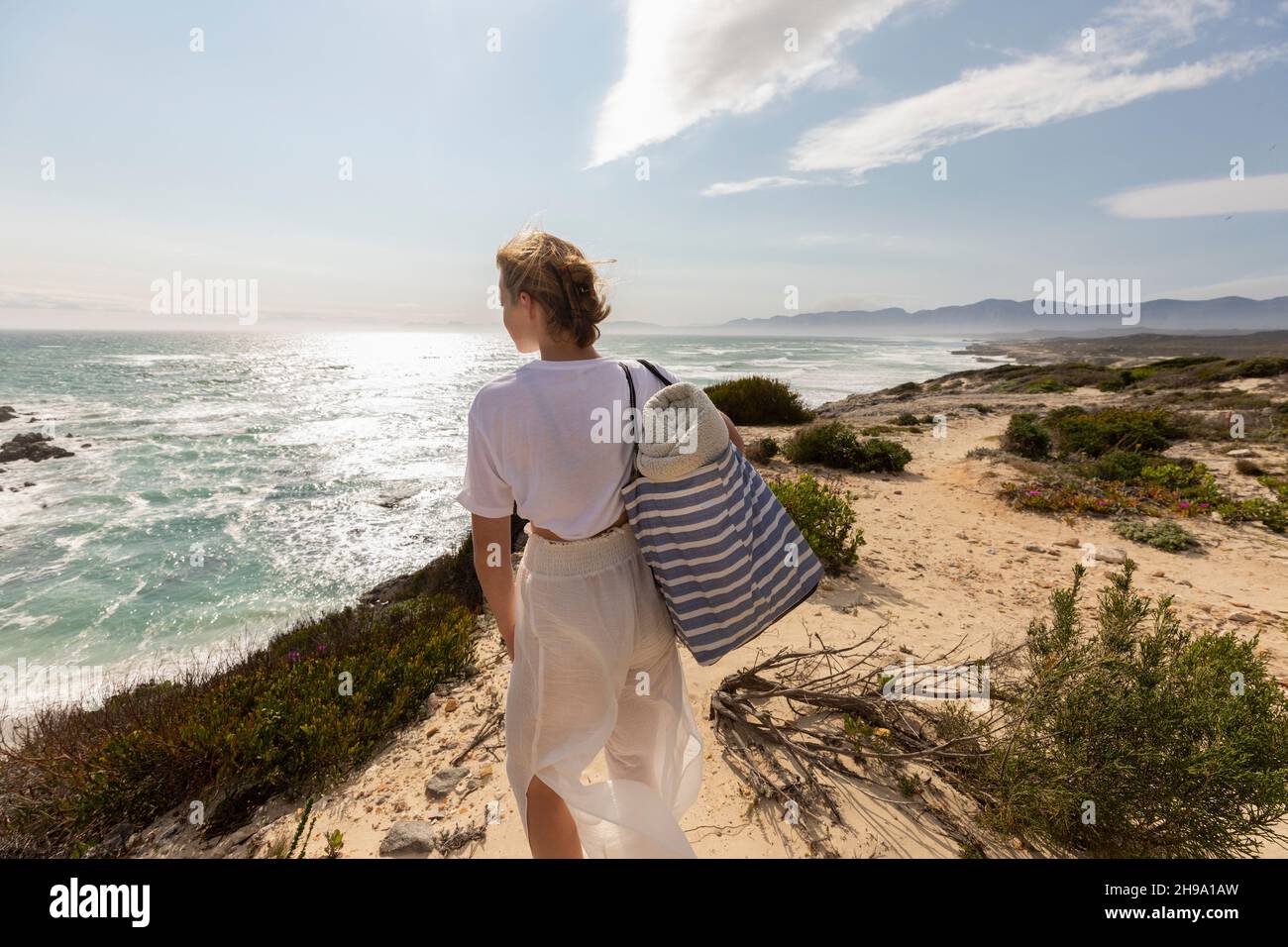 Teenage girl standing on top of a cliff looking over the coastline and ...