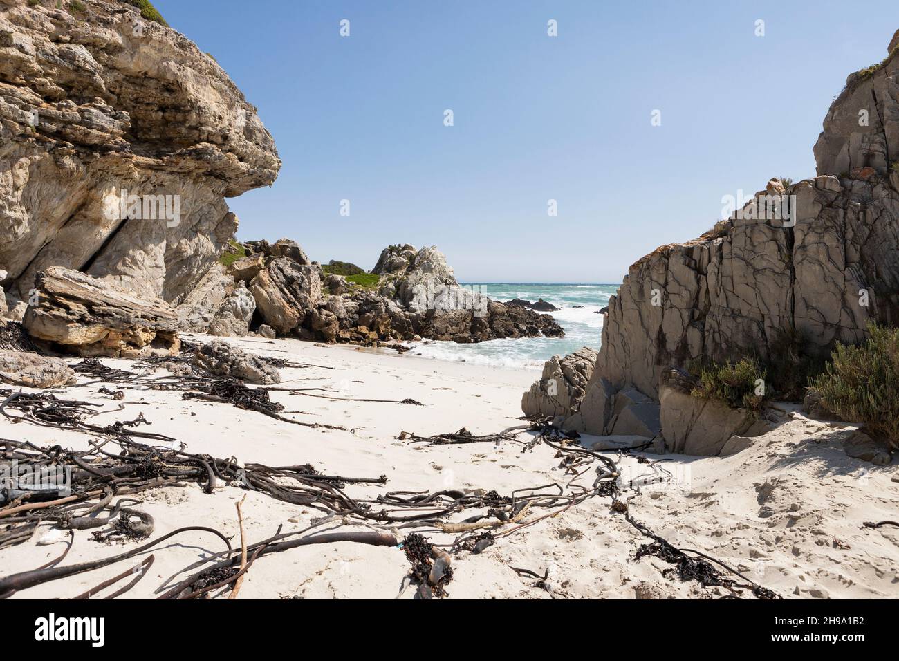 Eroded rock strata and jagged rocks looming over a small sandy beach ...