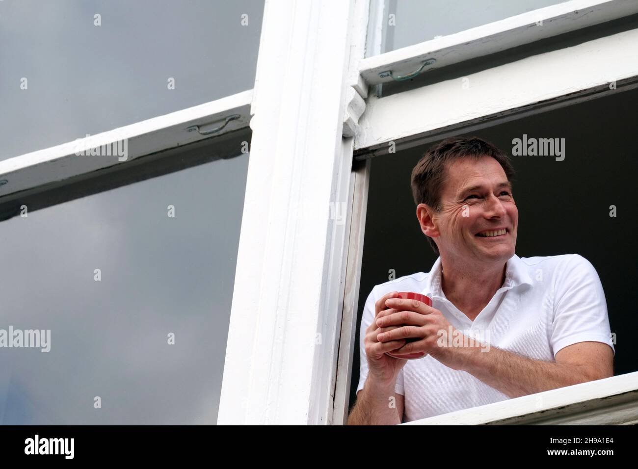 Smiling man leaning out of window holding hot drink Stock Photo - Alamy