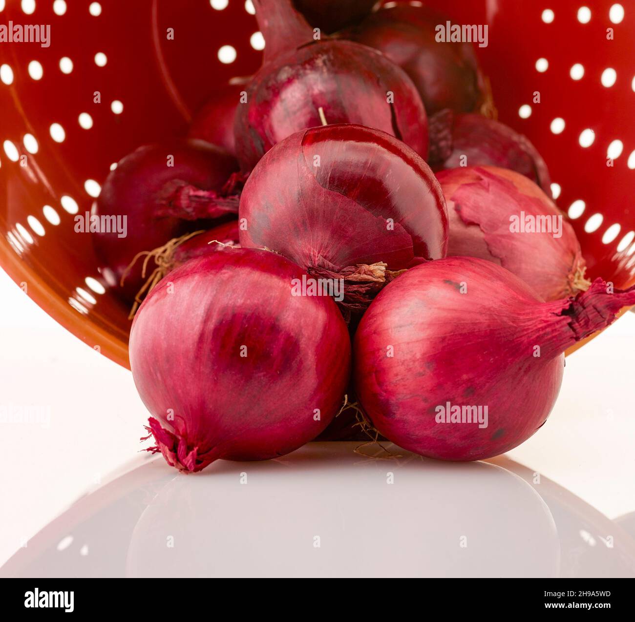 Close-up food still life with Red Onions rolling out of a red collinder ...