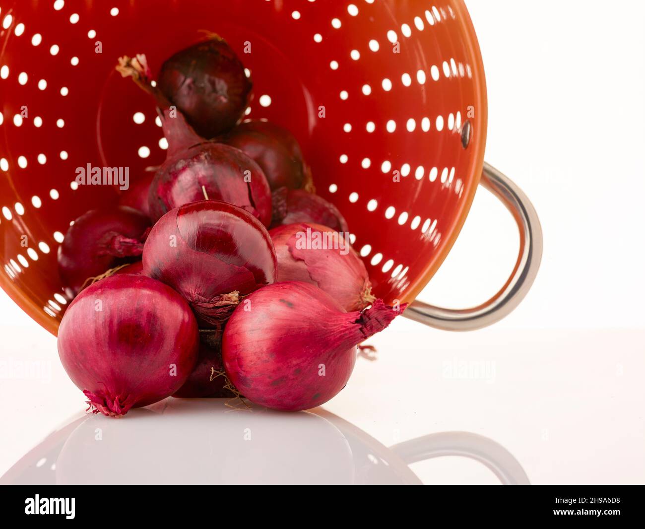 Close-up food still life with Red Onions rolling out of a red collinder ...
