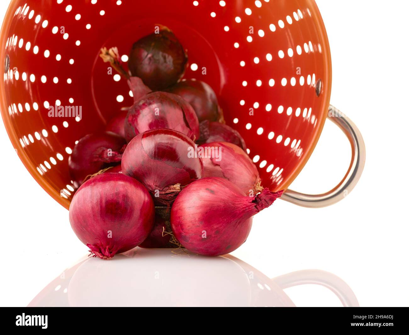 Close-up food still life with Red Onions rolling out of a red collinder ...