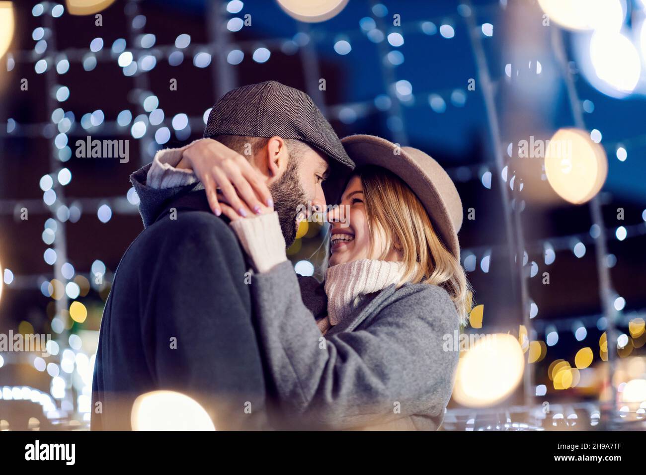 Christmas couple hugging on the street surrounded by lights on ...