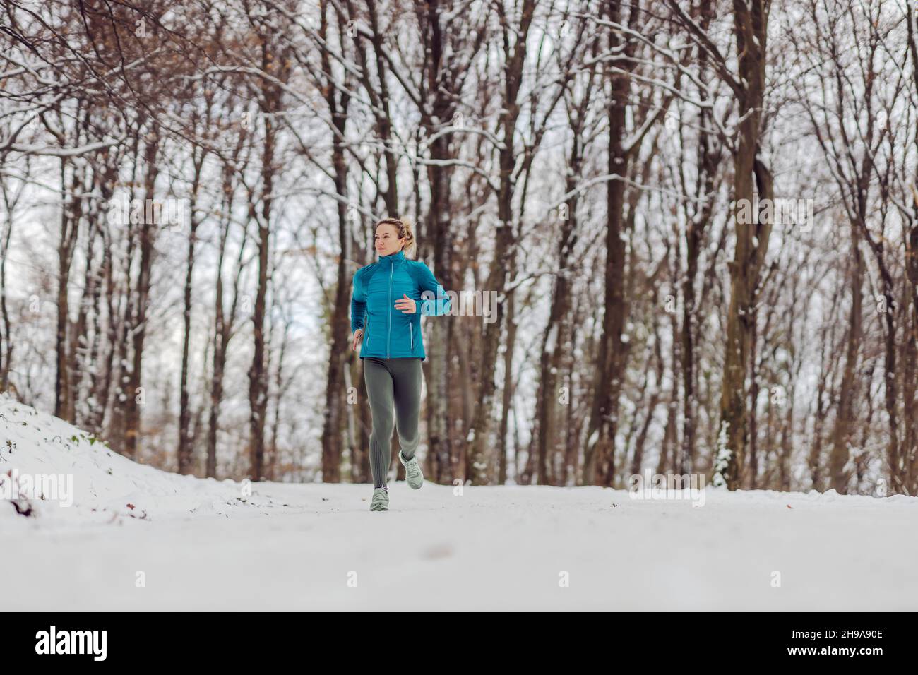Slim sportswoman jogging in forest on a snowy weather. Cold weather ...