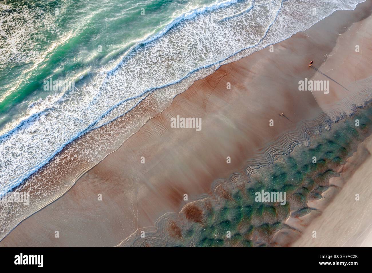 Aerial of Florida beach with a woman walking on wet sand between aqua ...