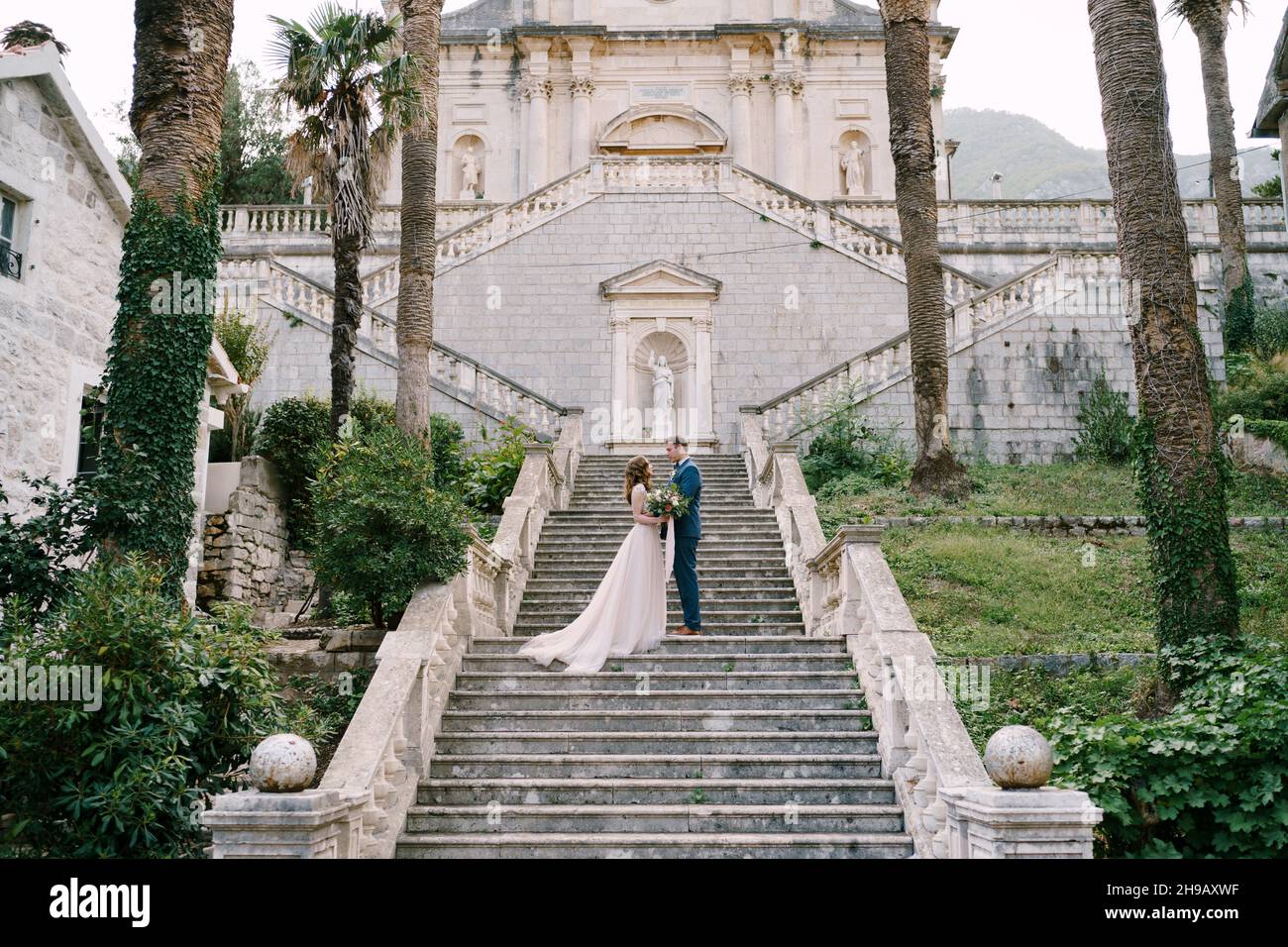 Bride and groom stand on the steps in the garden of the church in ...