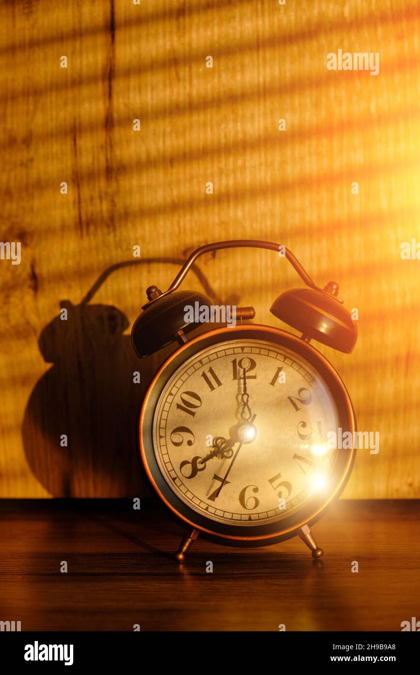Old retro alarm clock in early morning on table, shadows from blinds on ...