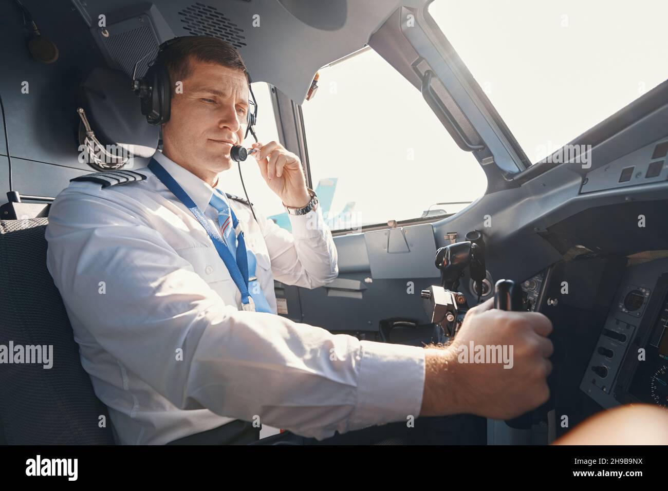 Male pilot in command controlling airplane while adjusting headset ...