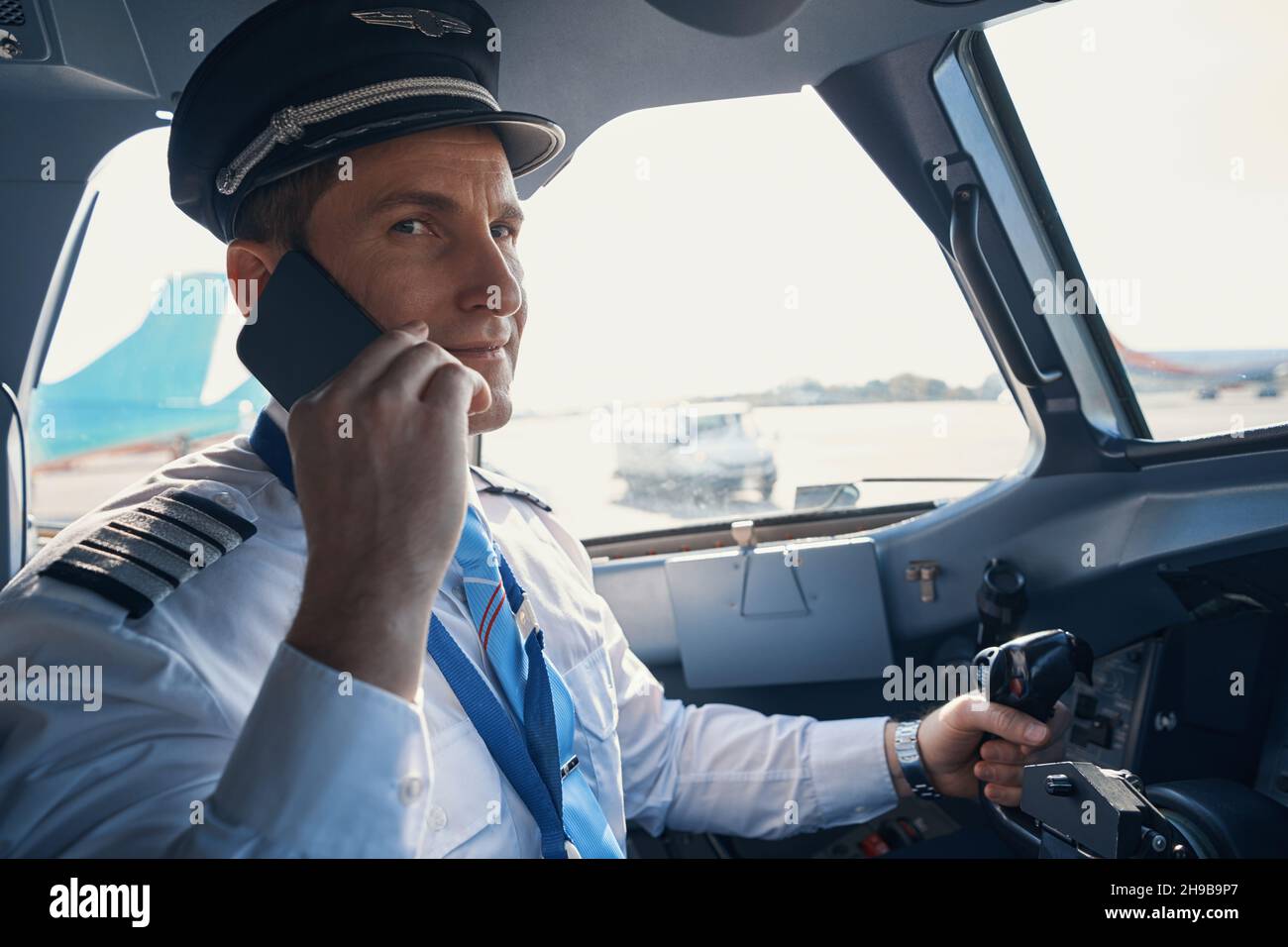 Captain of airplane taking on the phone while holding hand on steering ...