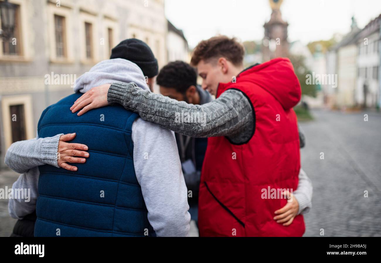 Rear view of community service volunteers hugging together outdoors in ...