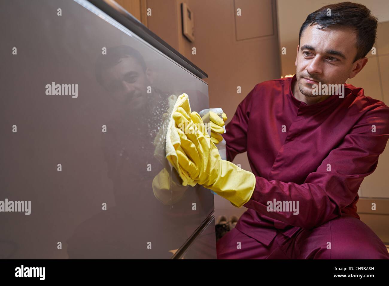 Male cleaner seated on haunches before piece of furniture wiping it ...