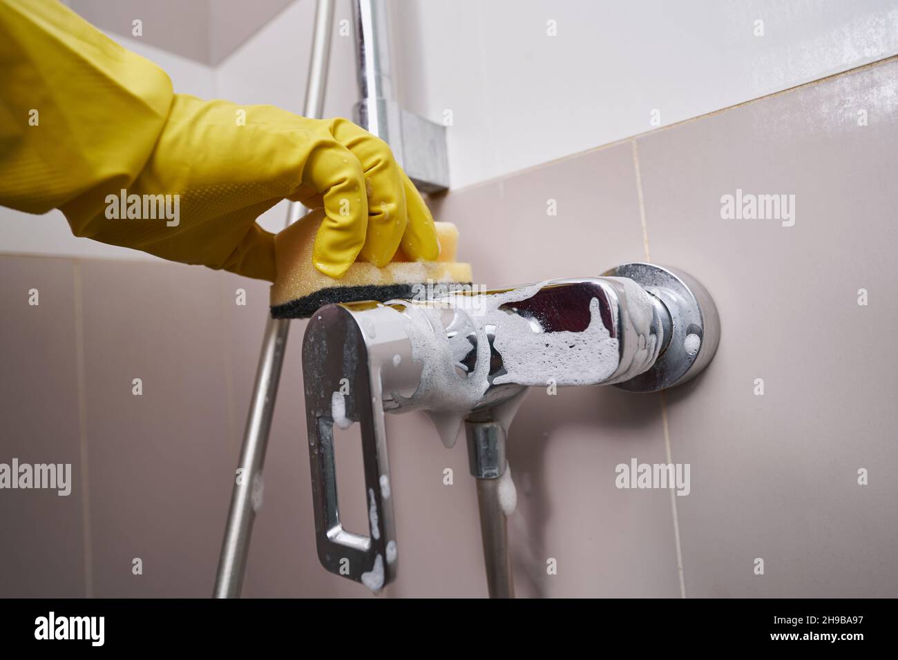 Cropped photo of gloved hand wiping chrome tap with soap solution and ...