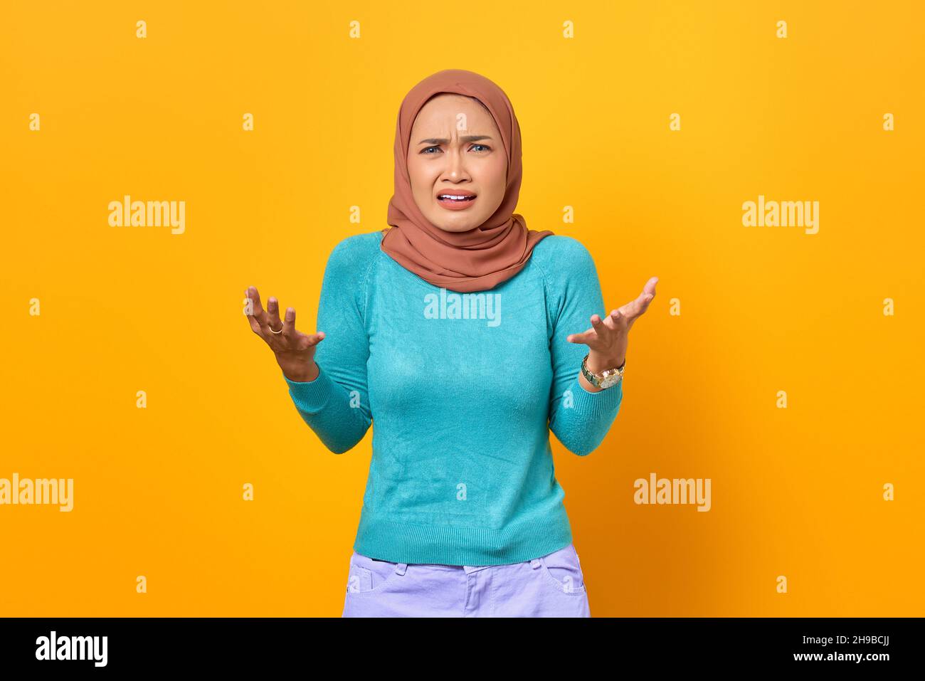 Confused young Asian woman shrugging raise hands on yellow background ...