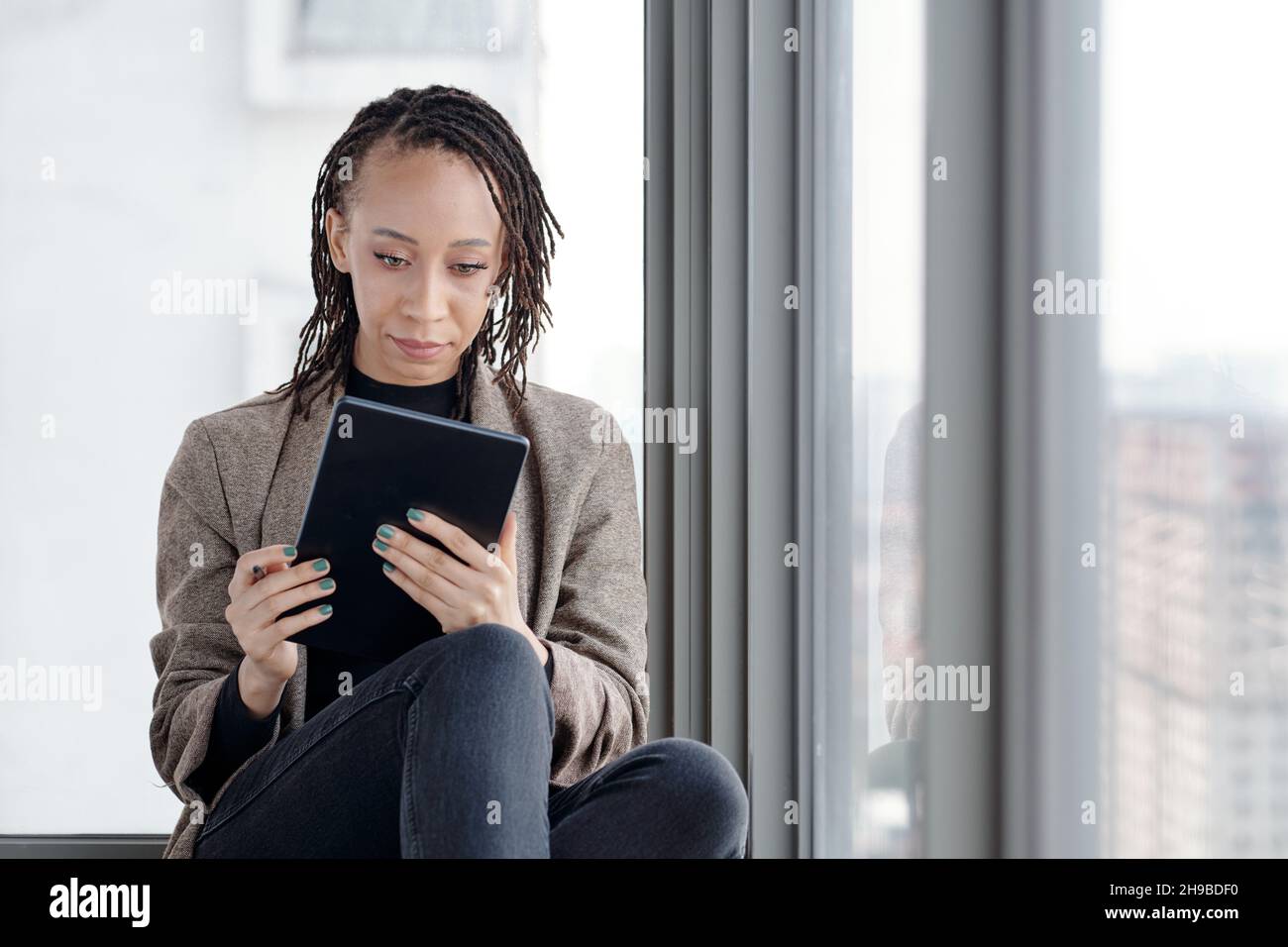 Pensive young woman sitting on window sill and drawing illustration on ...