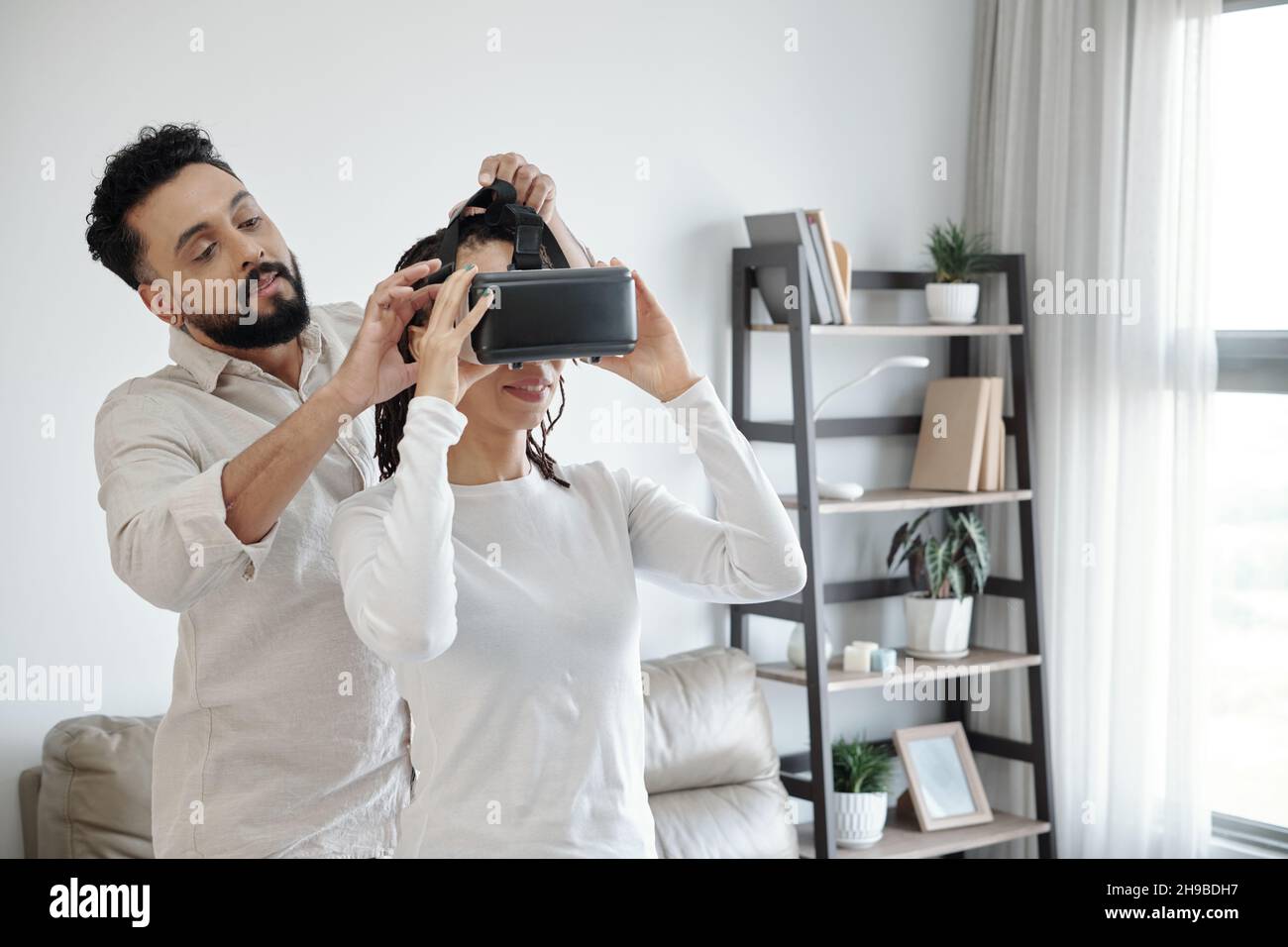 Handsome young man helping girlfriend to wear virtual reality headset ...