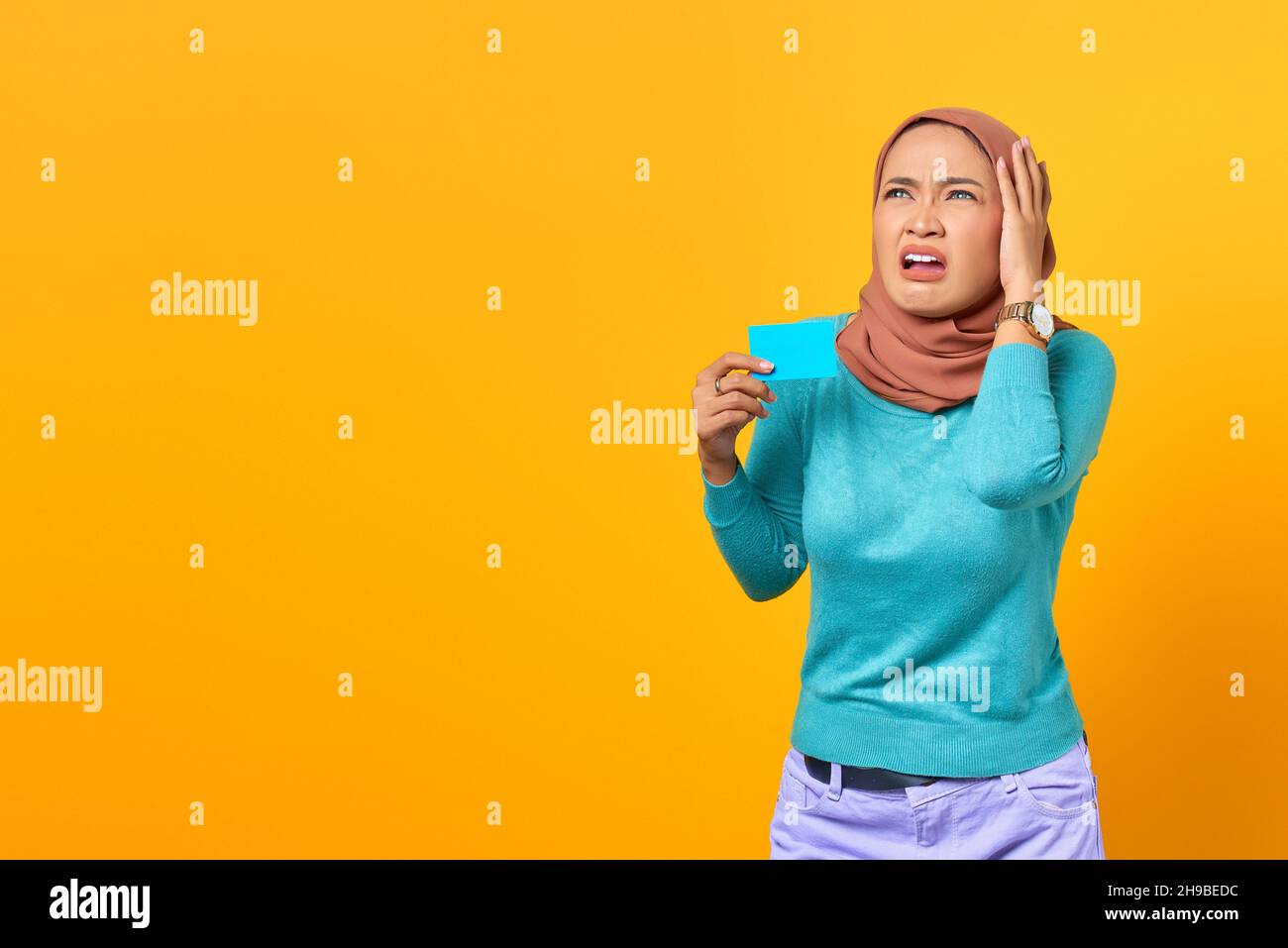 Shocked young Asian woman holding credit card and looking at copy space ...