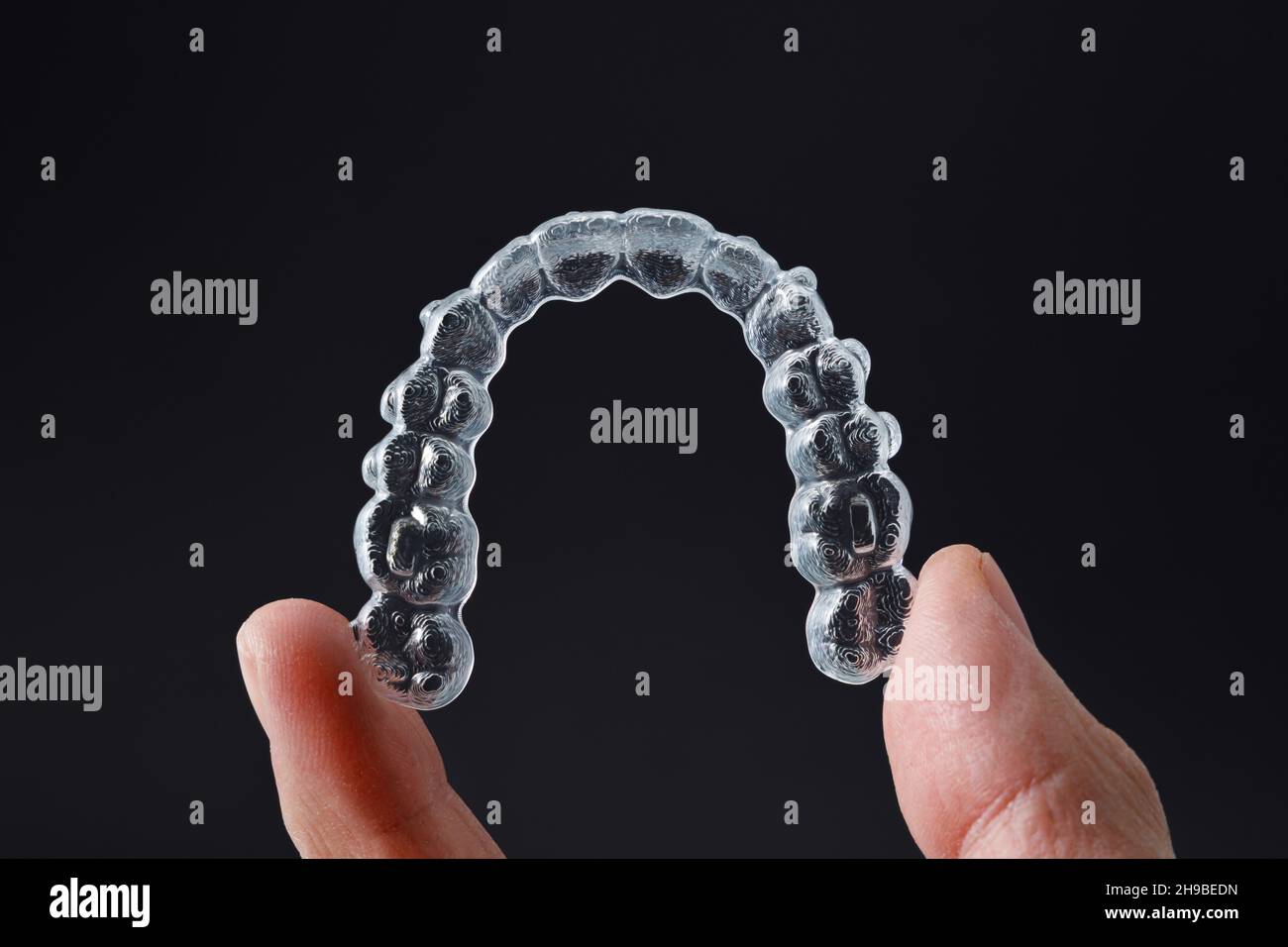 Hand holding one transparent retainer on black background. Invisalign ...