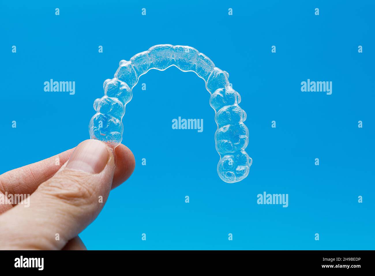 Hand holding one transparent retainer on blue background. Invisalign ...