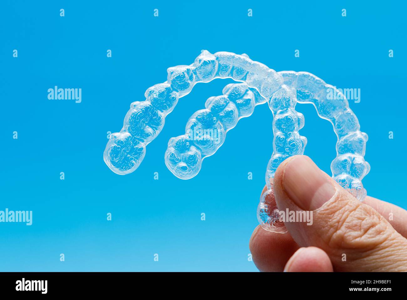 Hand holding two transparent retainers on blue background. Invisalign ...
