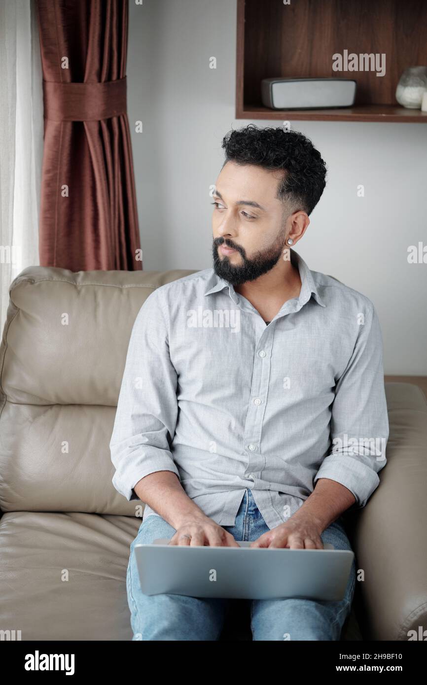 Software developer sitting on couch at home, coding on laptop and ...