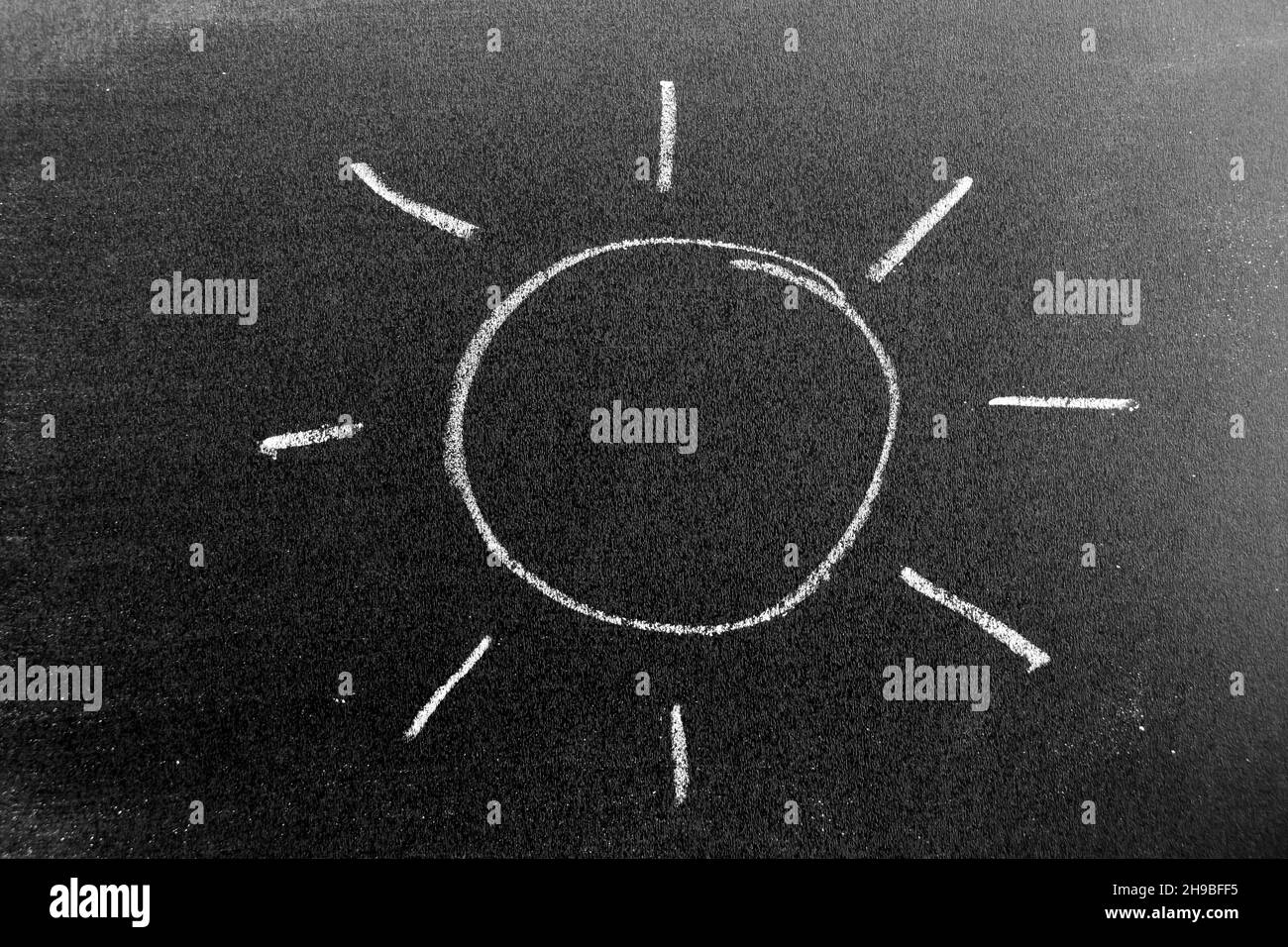 White color chalk hand drawing in sun with ray shape on black board ...