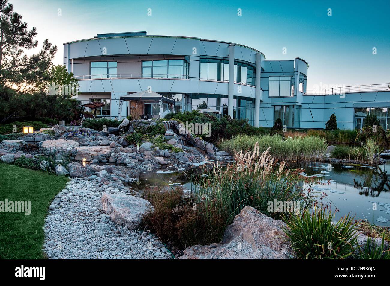 Evening summer view of modern two-story mansion with decorative pond in ...