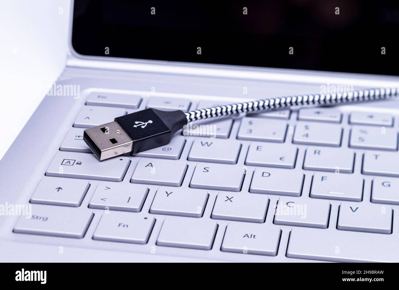 The photo shows a notebook with a USB cable positioned on the keyboard ...