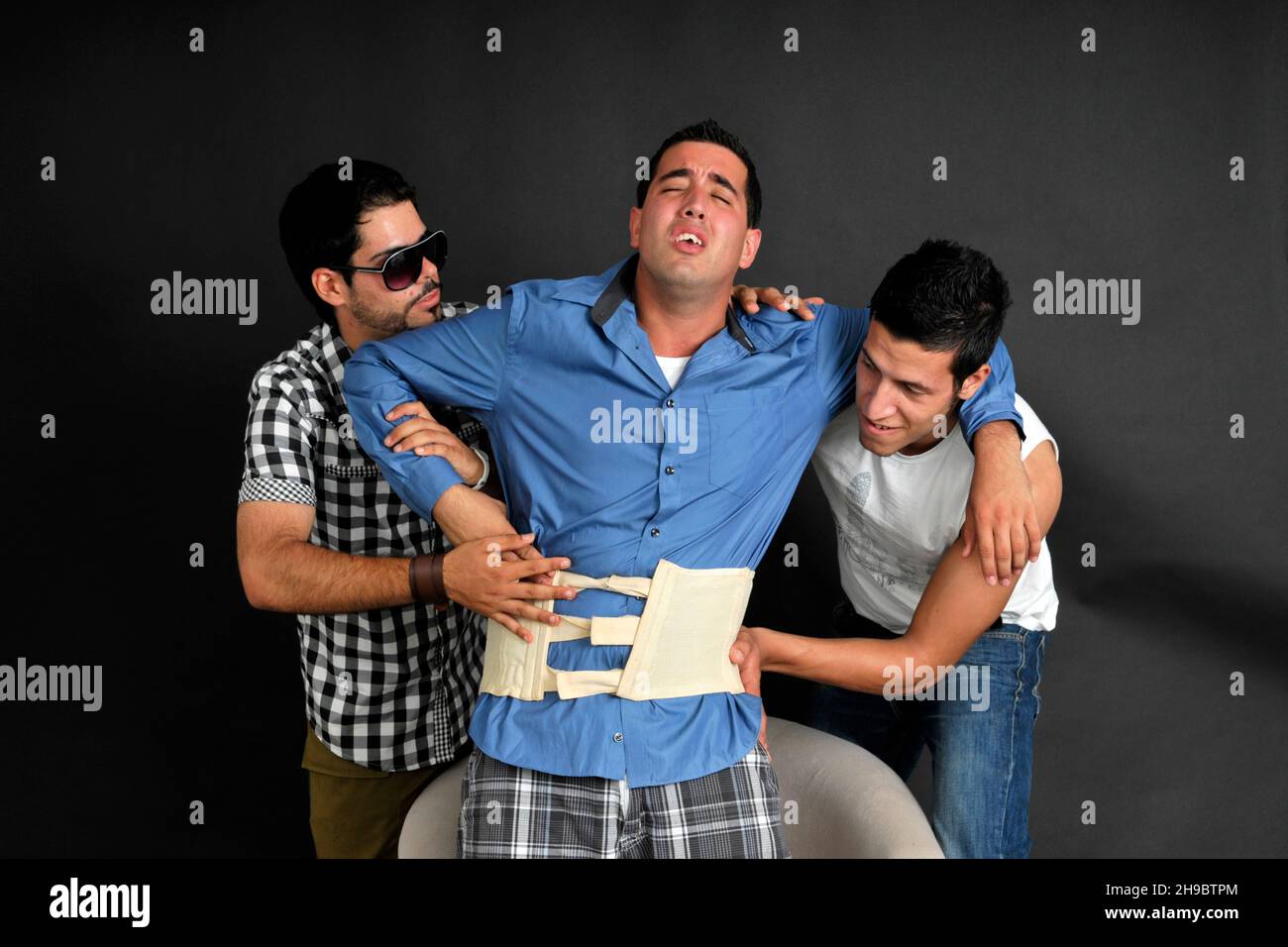 a young man suffering lower back pain is helped by his friends Stock ...