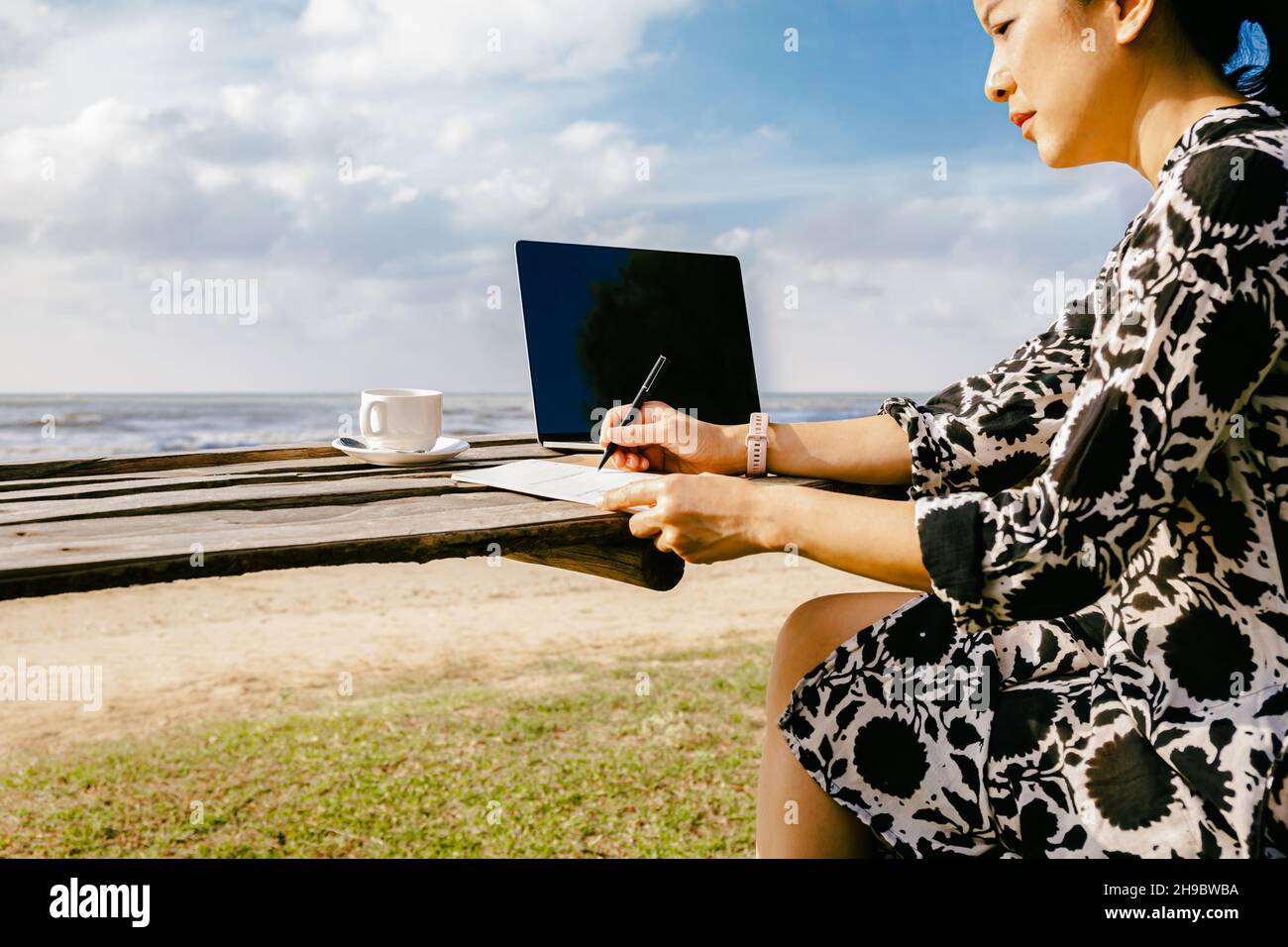 Woman working on laptop by the beach with hand writing in paper notebook on vacation Stock Photo ...