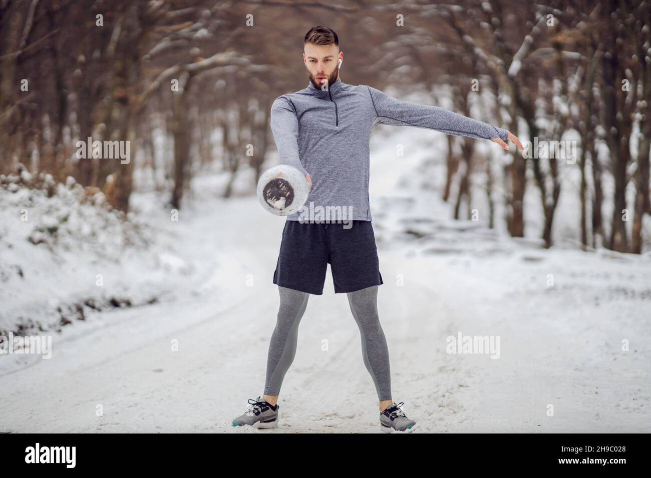 Fit bodybuilder standing on snowy path in forest and swinging ...