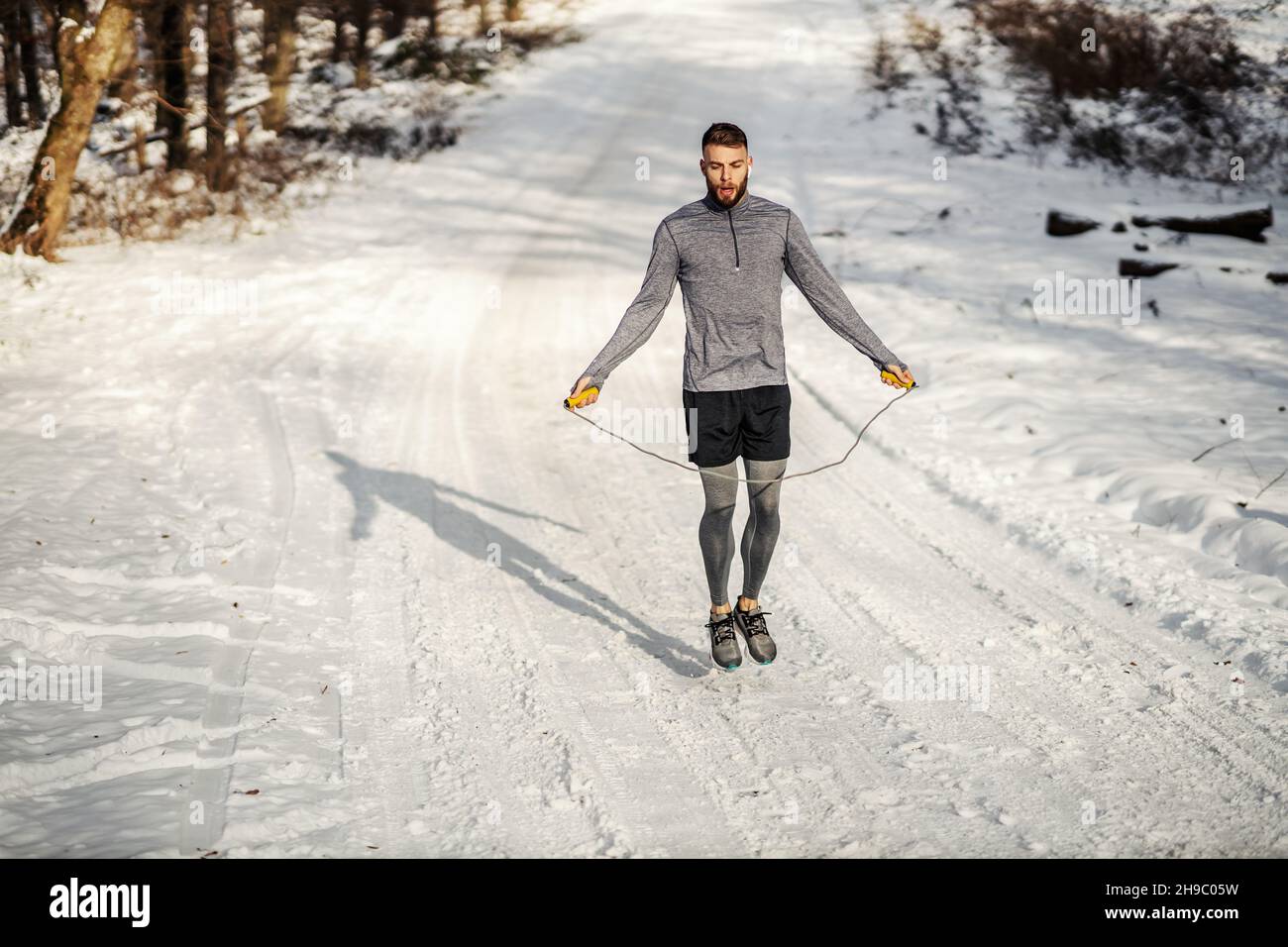 Fit sportsman jumping the rope in woods at snowy winter day. Winter ...