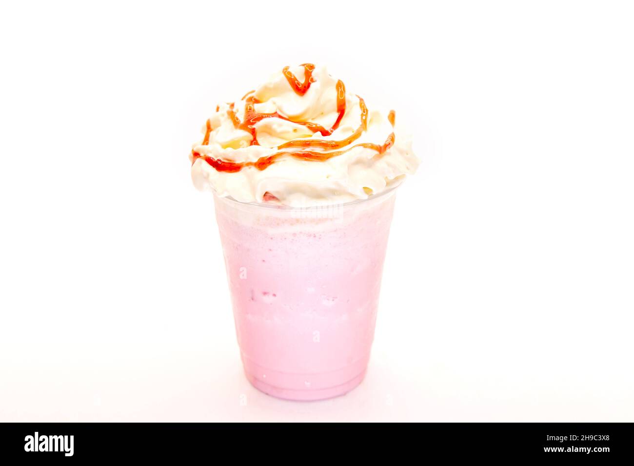Strawberry milk shake with syrup drizzled on whipped cream in a plastic ...
