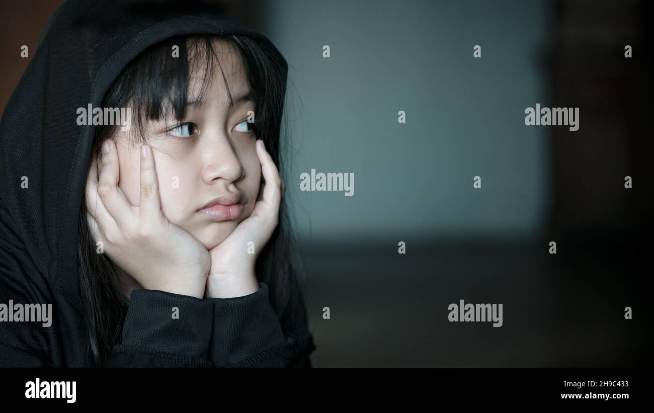Sad lonely little girl crying while sitting in dark room with an ...