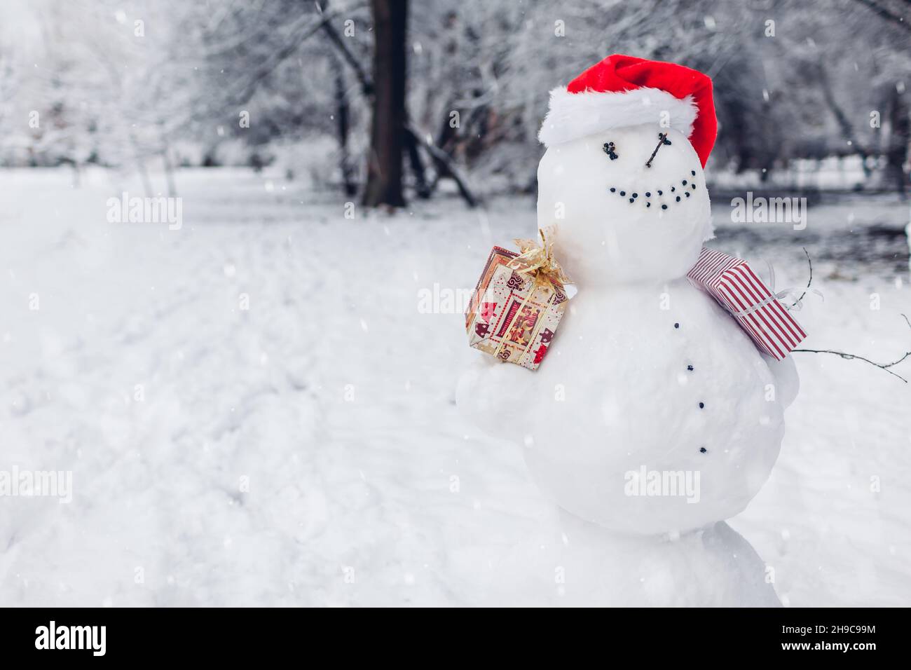 Happy snowman wearing festive Santa hat in snowy winter park at ...