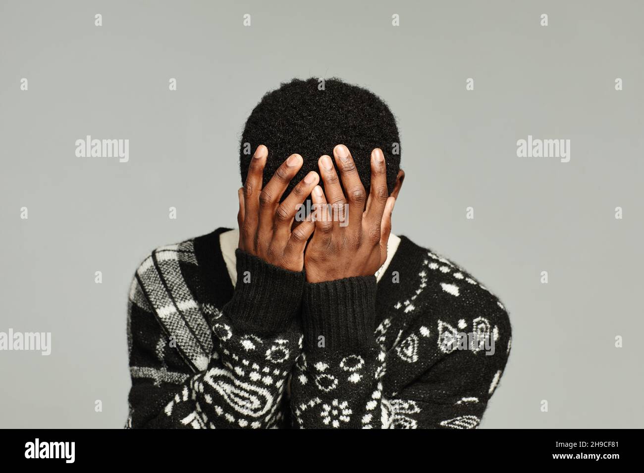 Portrait of anonymous African American man hiding face against grey ...