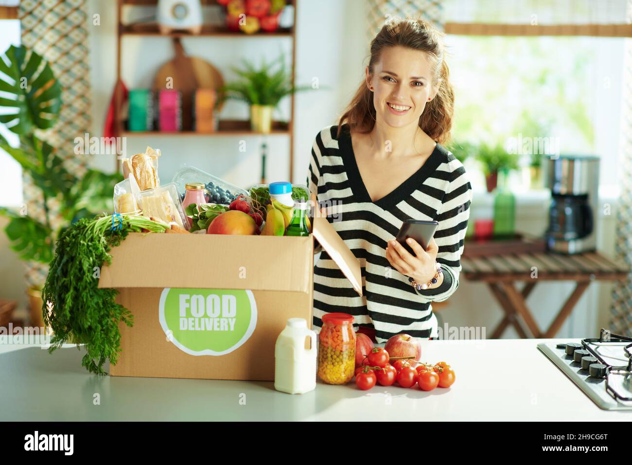 Food delivery. happy young female with food box in the kitchen using ...