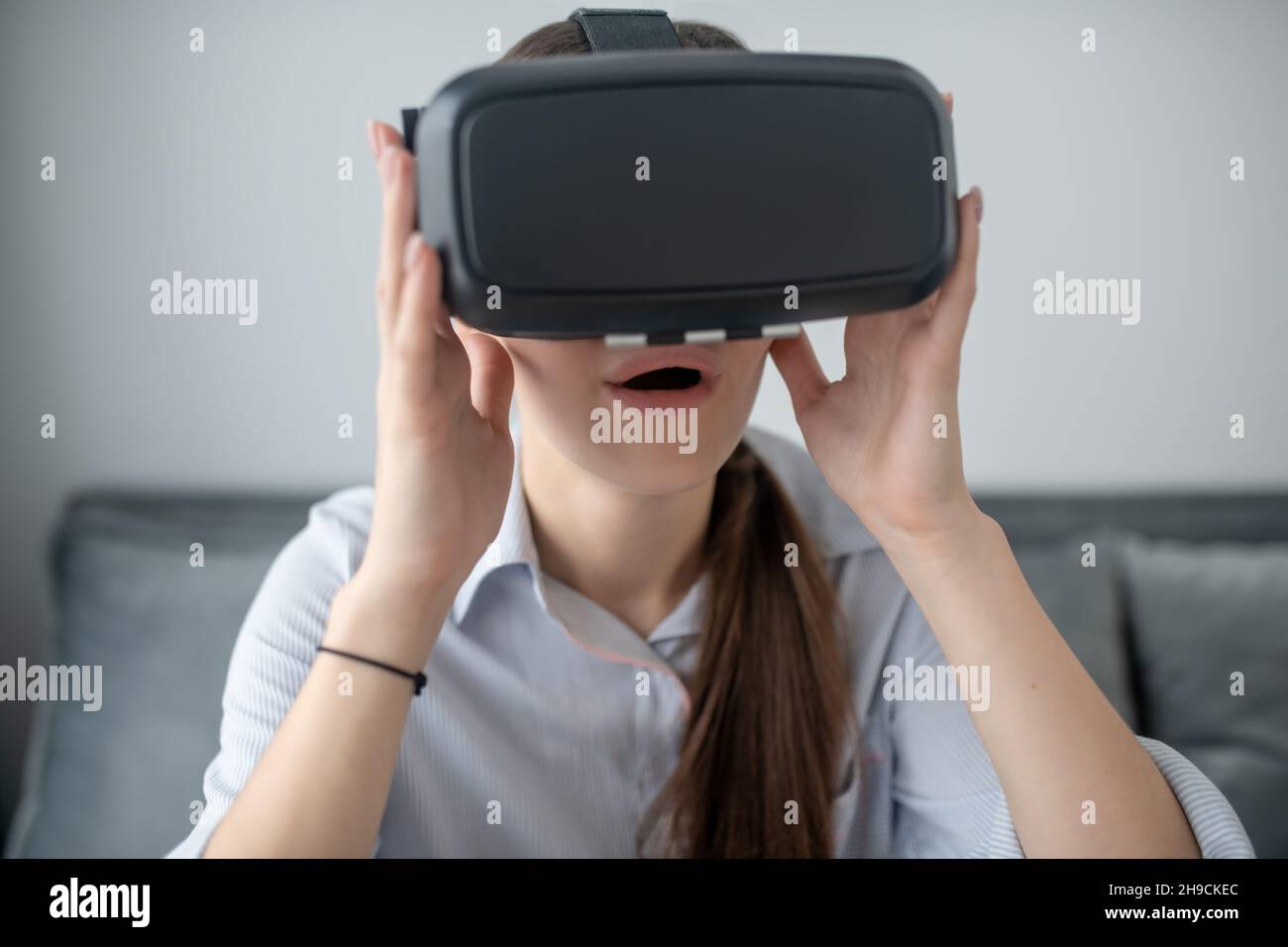 Astounded lady seated in a room playing a 3D game Stock Photo - Alamy
