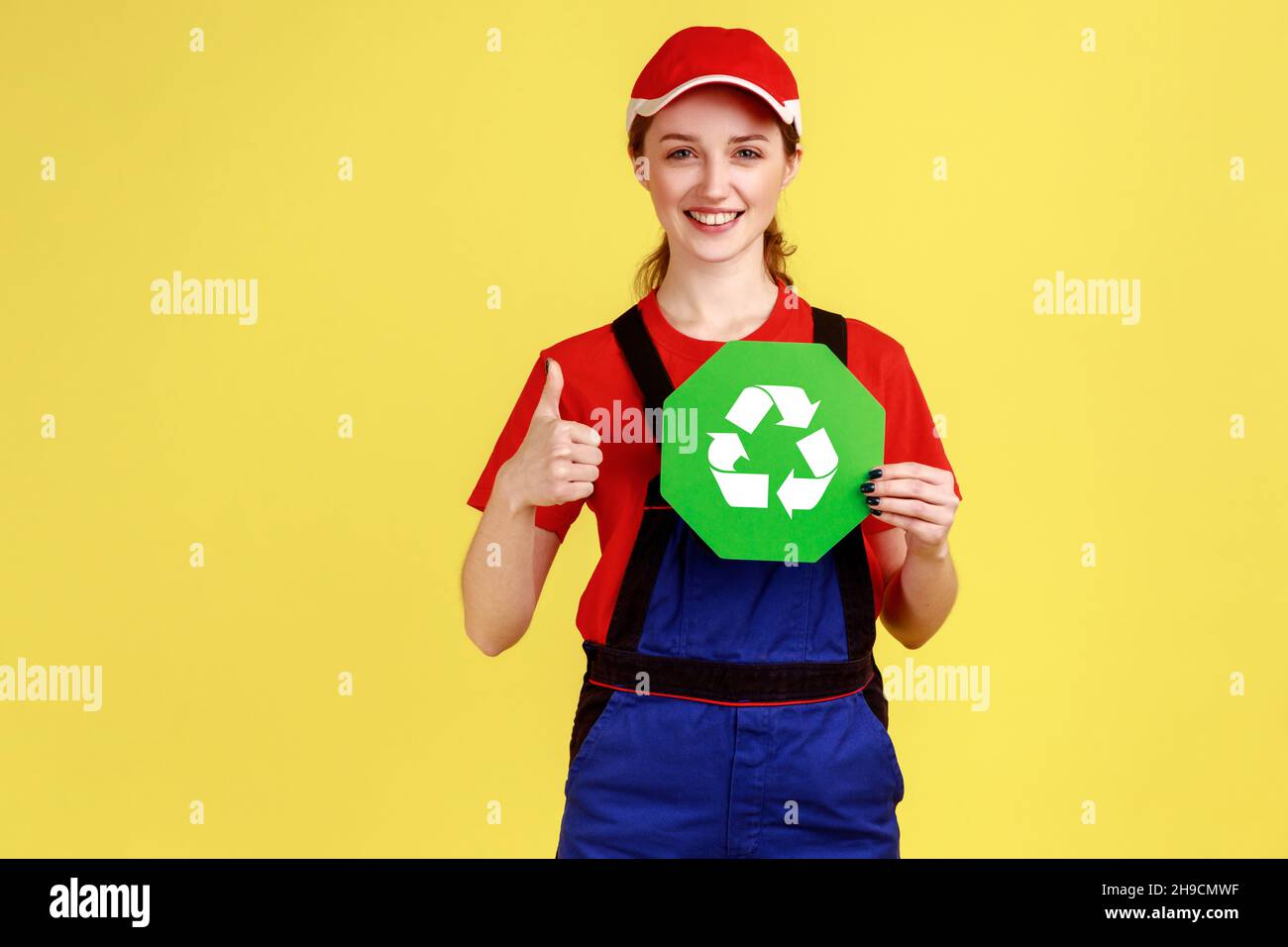 Portrait of optimistic worker woman standing and holding recycling sign ...