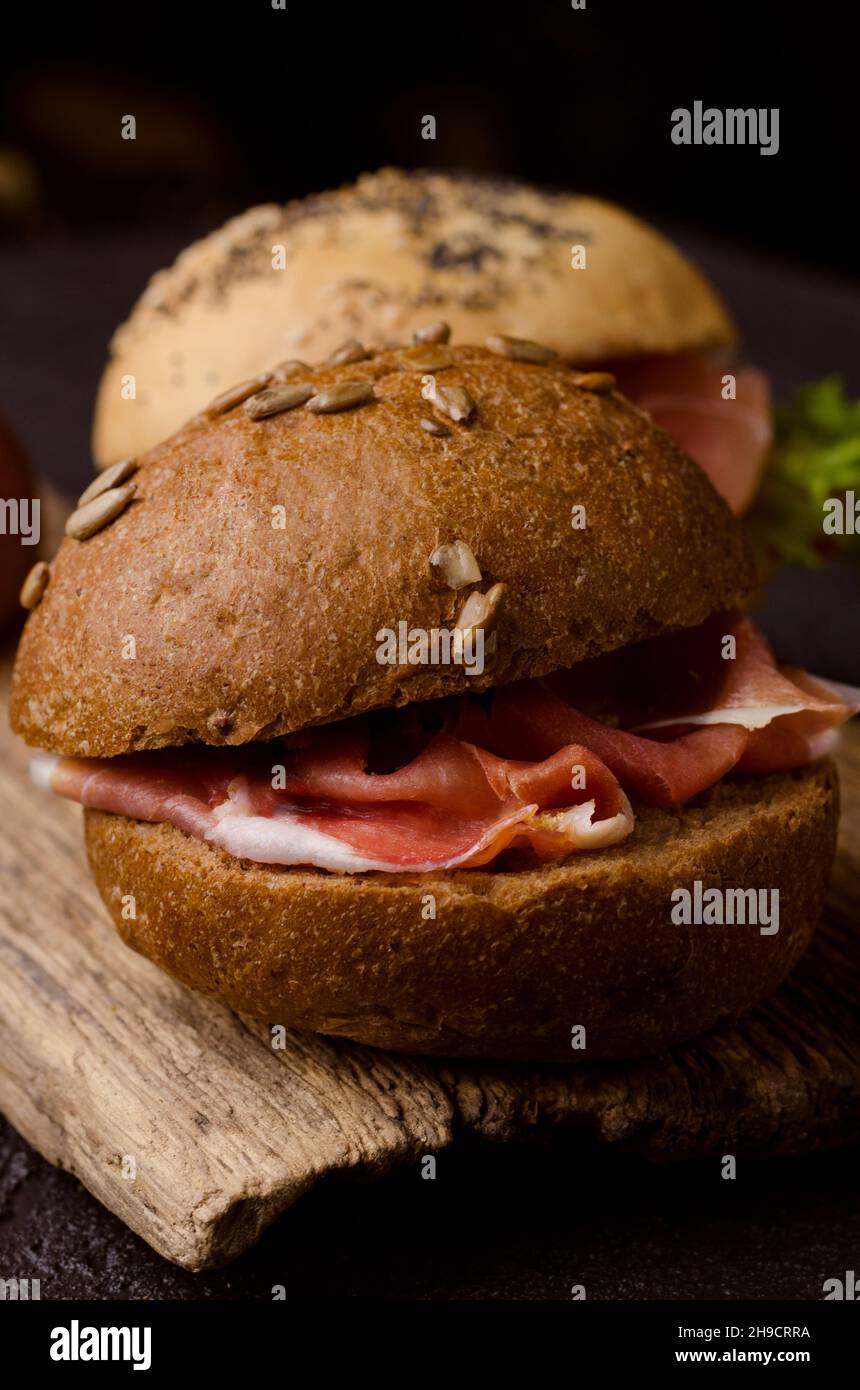 Delicious crispy burger bun with sliced ham on a vintage wooden cutting ...
