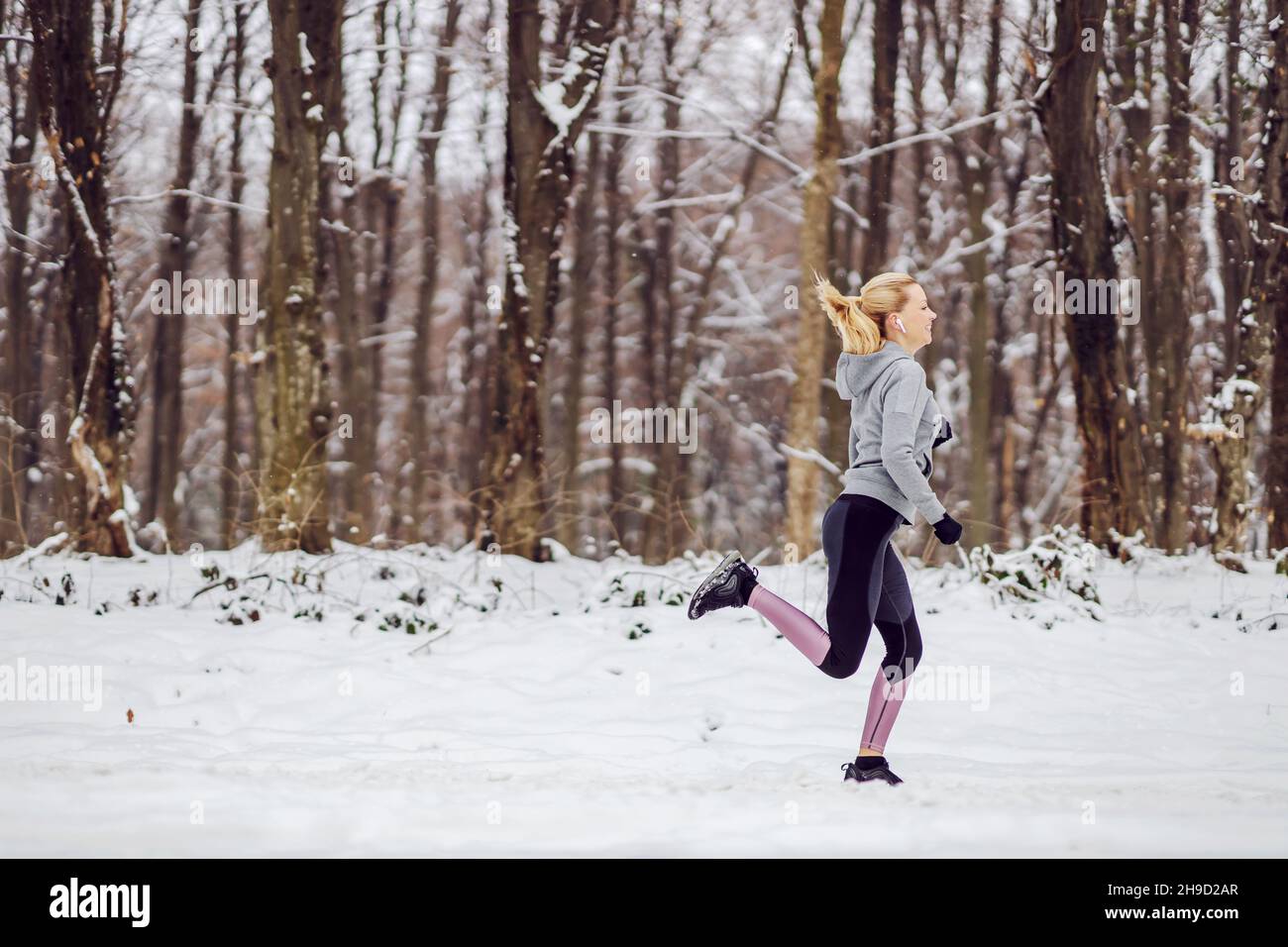 Happy fit sportswoman jogging in nature on snowy path at winter ...