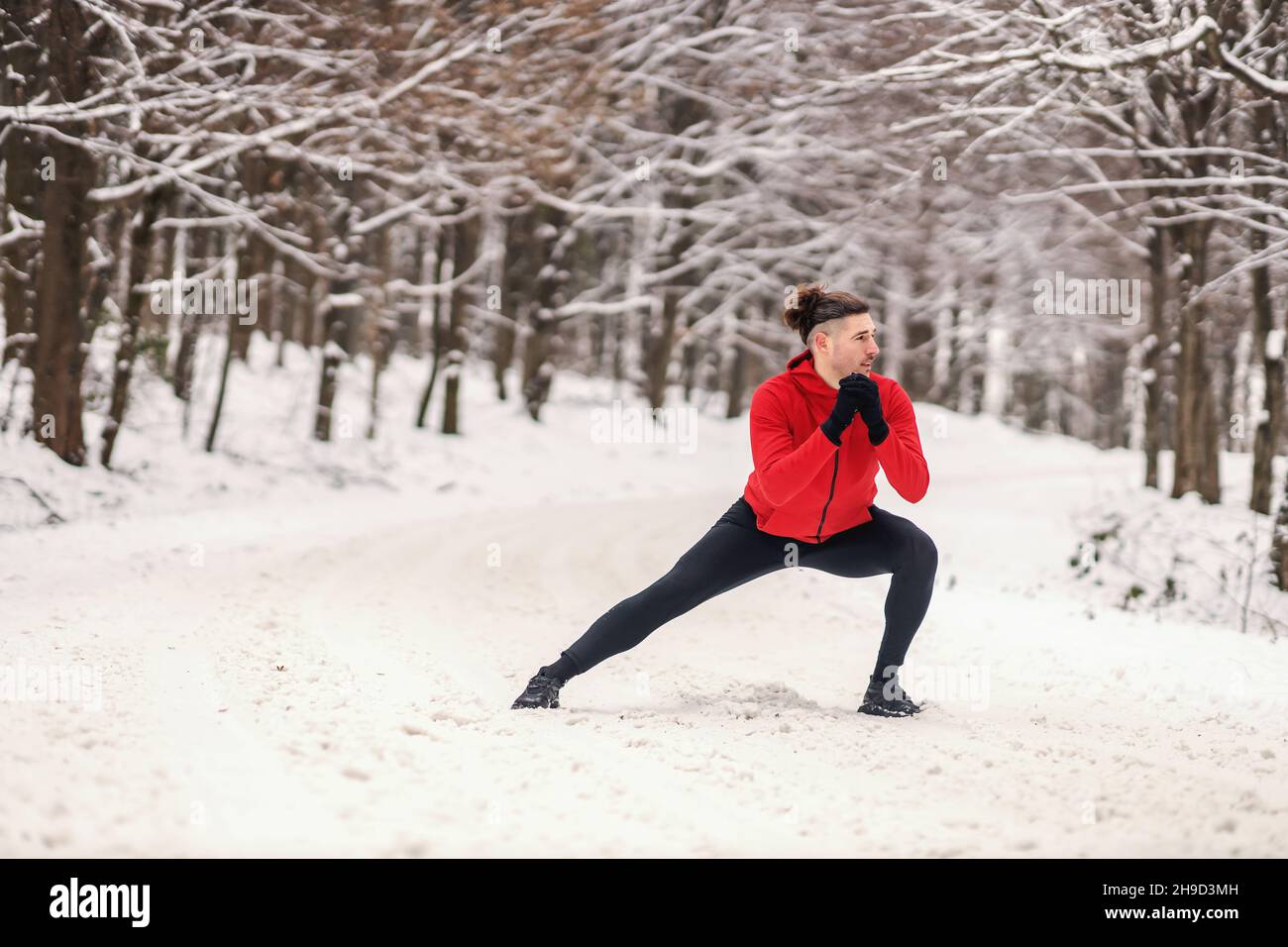 Sportsman doing stretching and warmup exercises while standing in snow ...