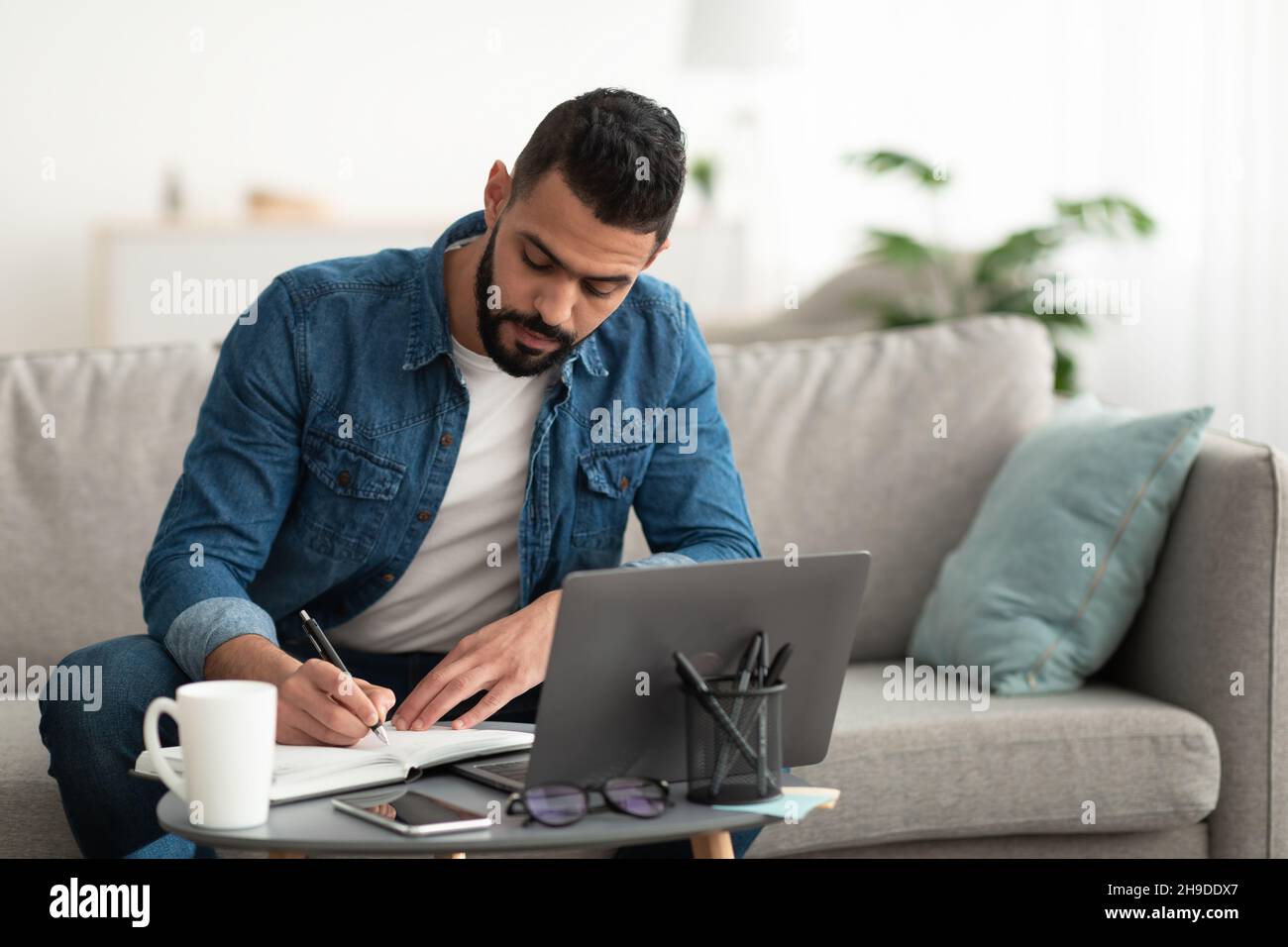 Focused young Arab man taking notes during remote business meeting ...