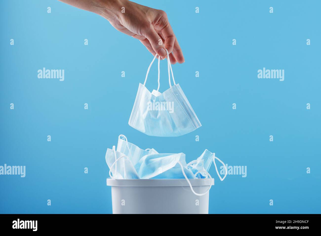 Hand throws a used face shield into the trash can on a light blue ...