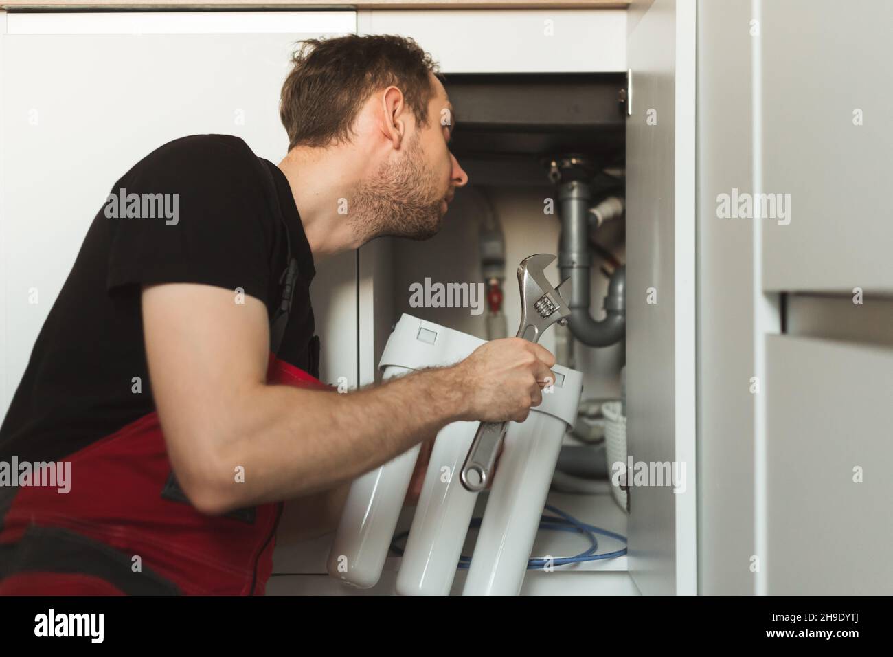 Plumber in the kitchen installs a household water treatment system ...
