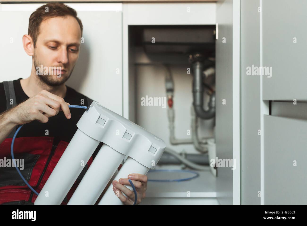Plumber in the kitchen installs a household water treatment system ...