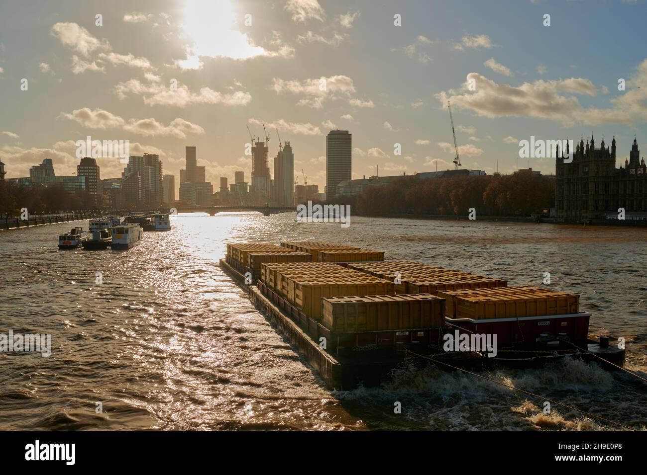 Barge on River Thames against low bright sun in blue sky with clouds ...