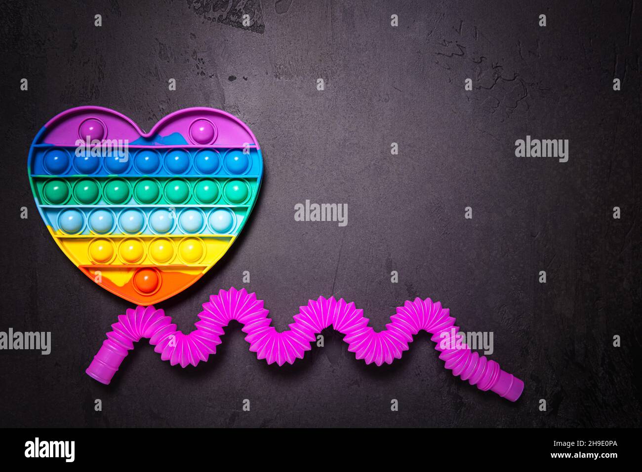 Flat lay with pop it rainbow heart and bent as wave pink pop tube toy ...