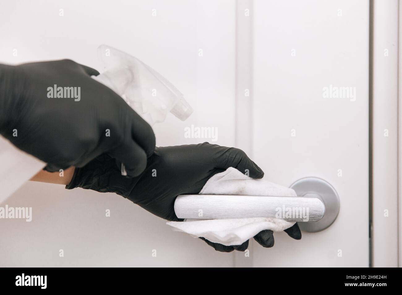 Cleaning door handle with dirty wipe in black gloves and sanitizer ...