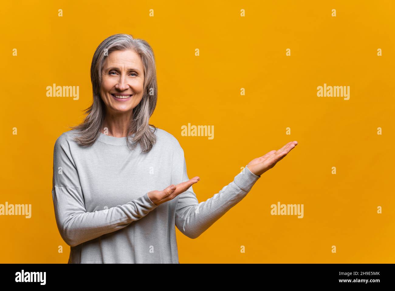 Satisfied modern mature woman presenting novelty isolated on yellow ...
