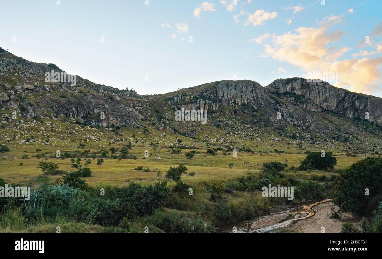 Green meadows with rocks, some trees, steep rocky cliffs background ...
